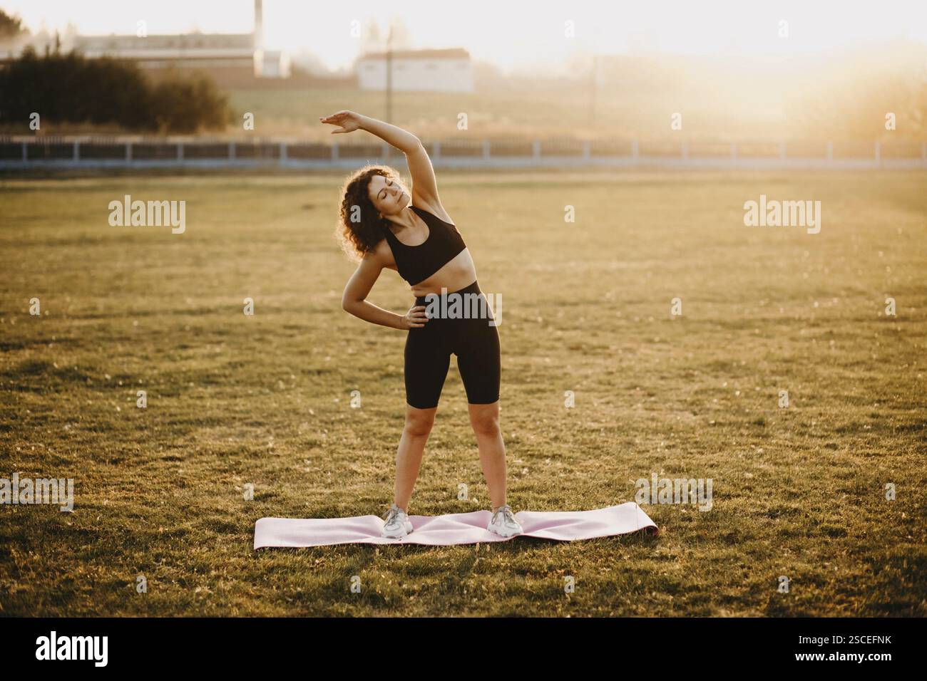 Woman performing a side stretch on a yoga mat in the open field Stock ...