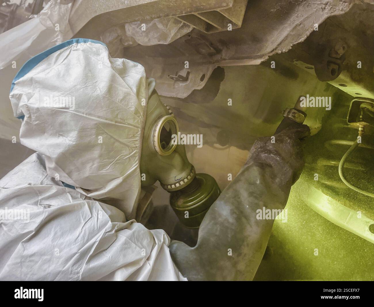 Person wearing a gas mask and suit inspecting car undercarriage with ...
