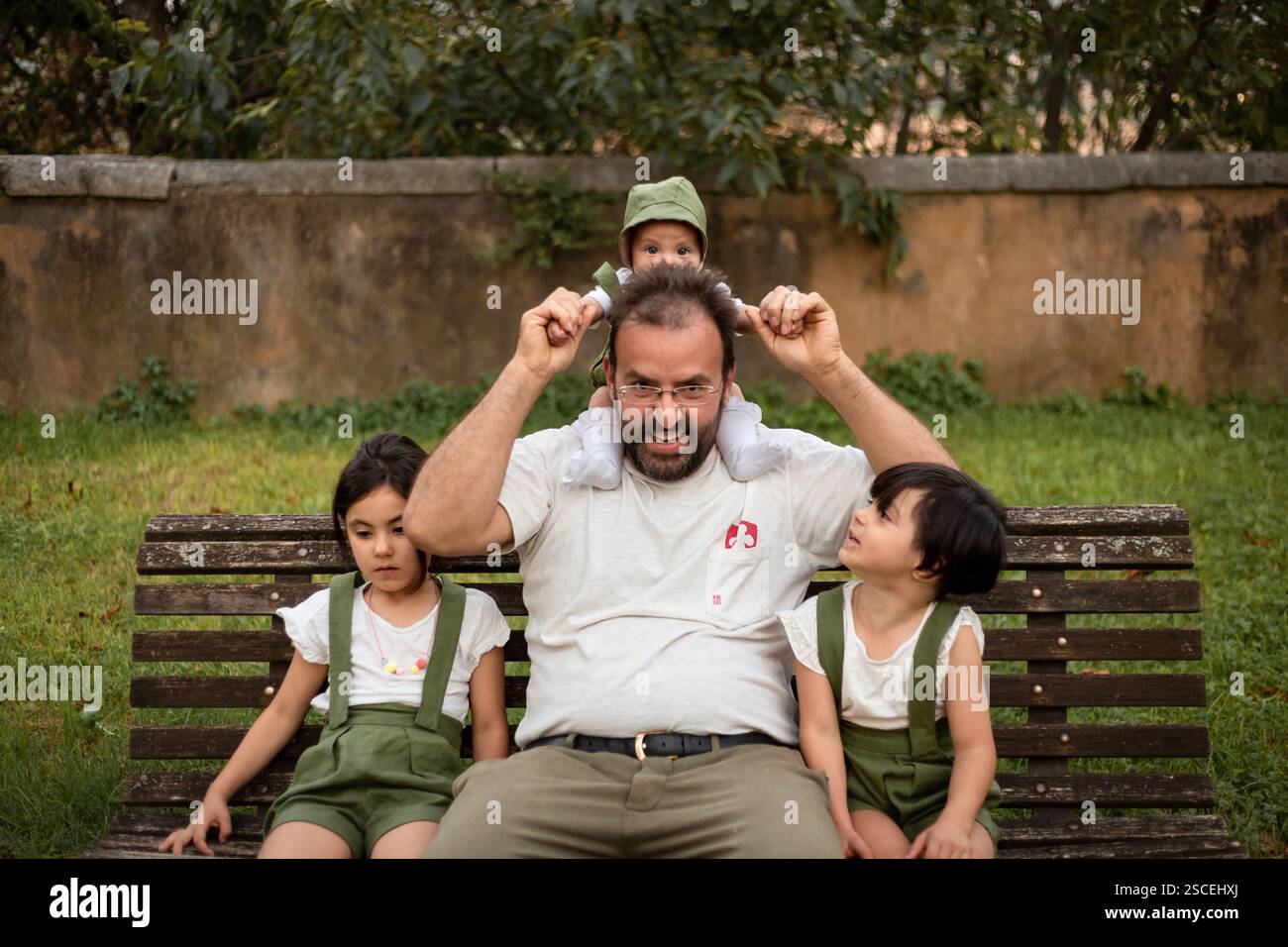 dad sitting with small baby and two elder children on the bench in the ...