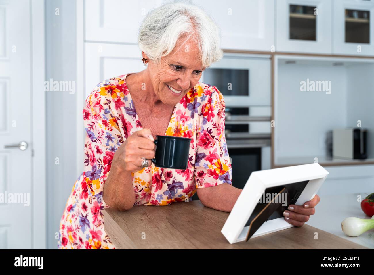 Beautiful senior old woman with gray hair at home look at a painting to ...