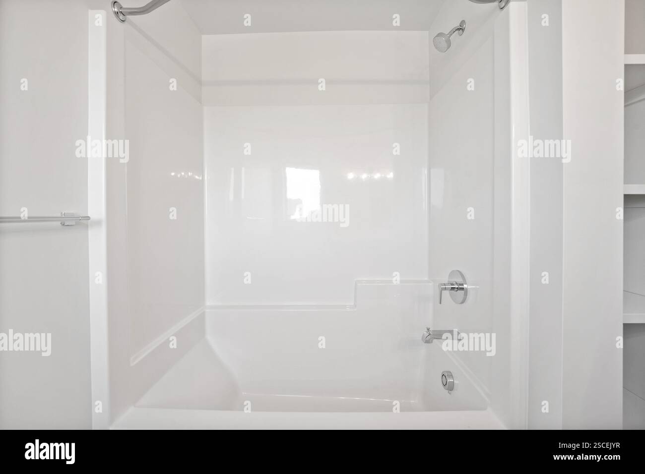 A white bathroom with a white tub and a white shower. The tub is empty ...