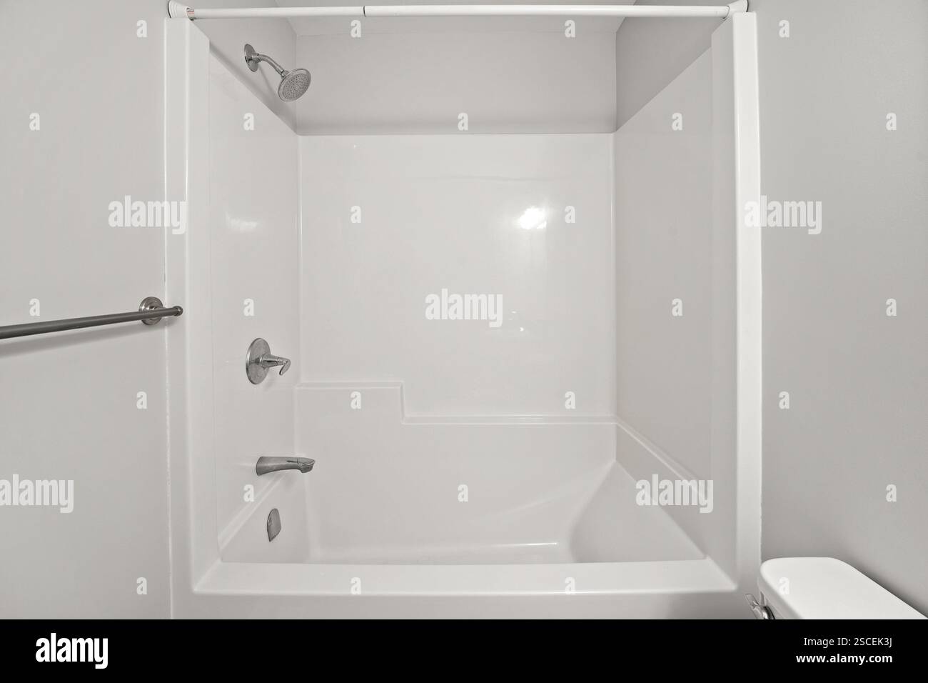 A white bathroom with a white tub and shower. The tub is empty and the ...