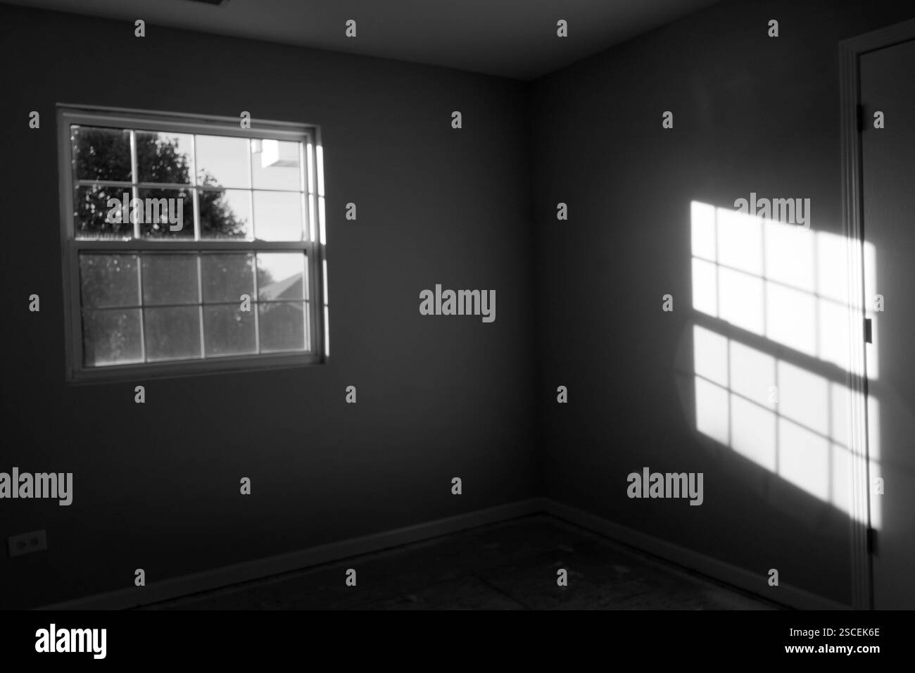 Afternoon light streams through a window onto a white wall in an empty ...