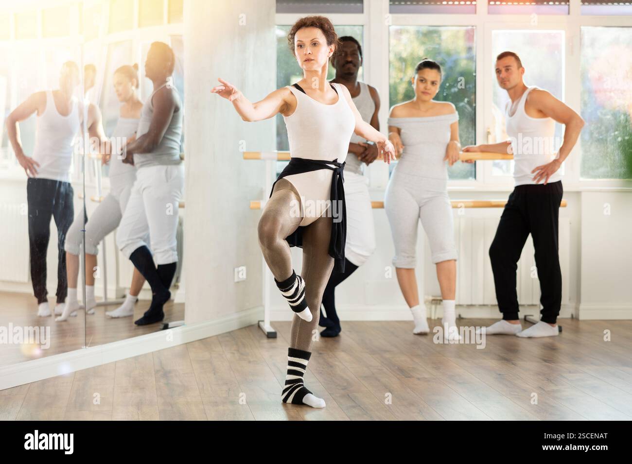 Female ballet instructor demonstrating movements to group of dancers ...