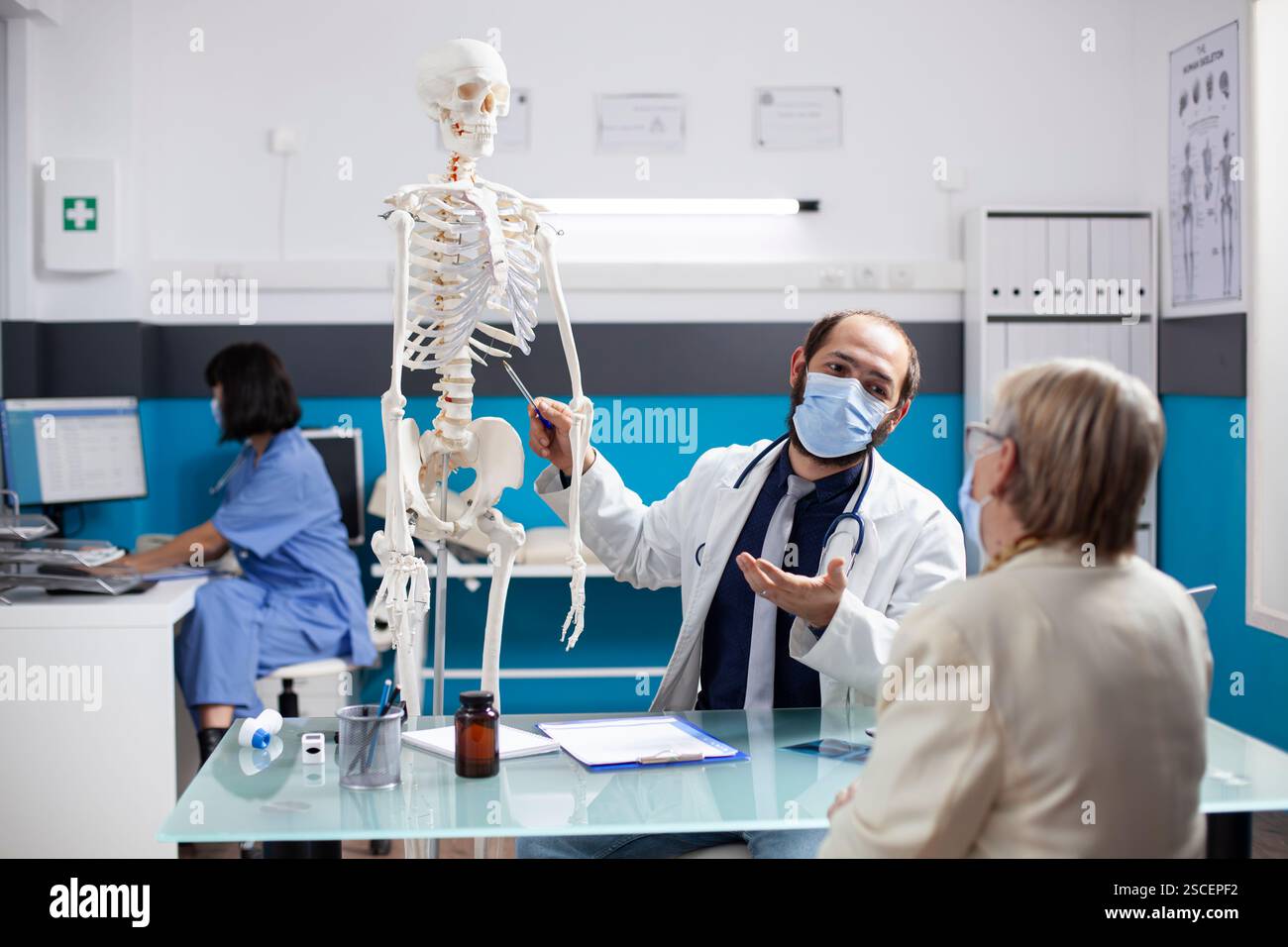 Doctor discussing spinal health with pensioner patient, using skeleton ...