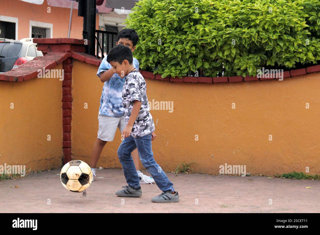 Two 9-year-old poor dark-skinned Latino boys play soccer in the street ...