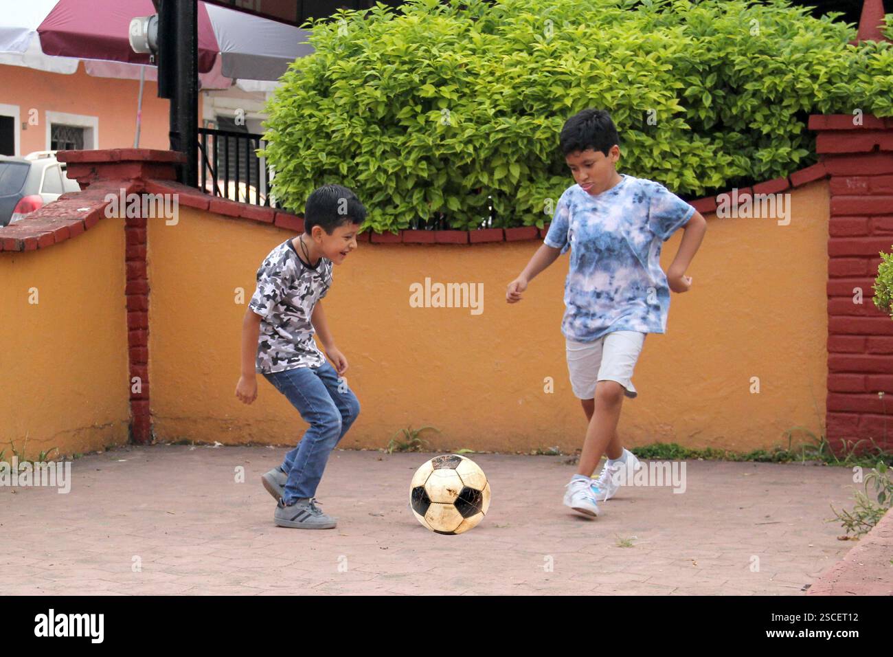 Two 9-year-old poor dark-skinned Latino boys play soccer in the street ...