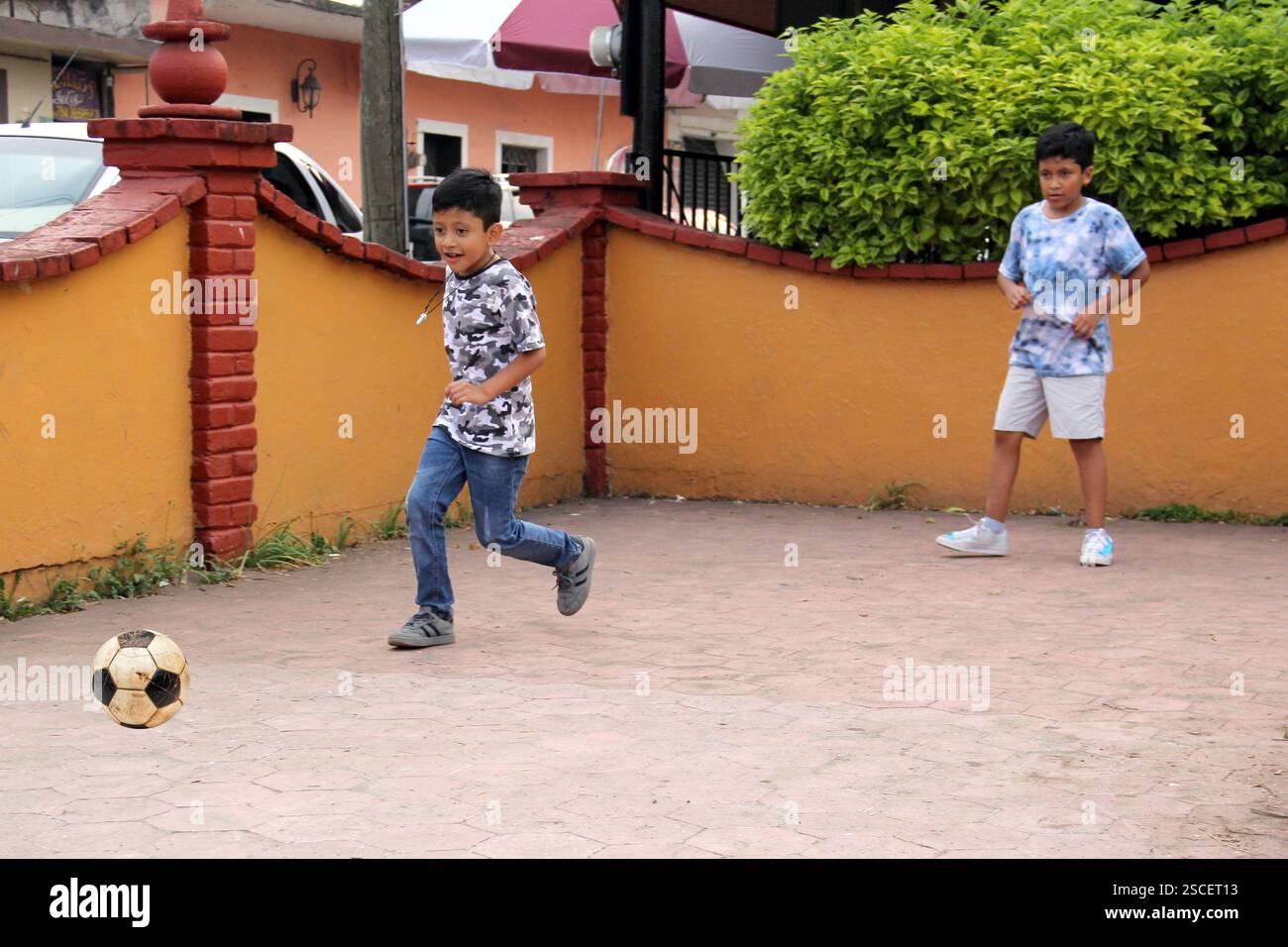 Two 9-year-old poor dark-skinned Latino boys play soccer in the street ...