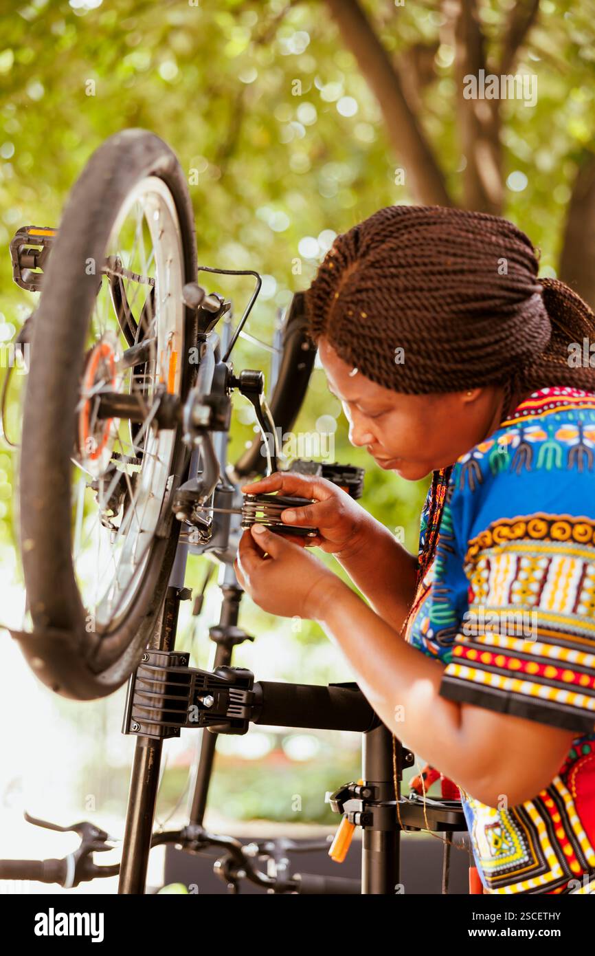 Young healthy african american woman doing maintenance on damaged bike ...