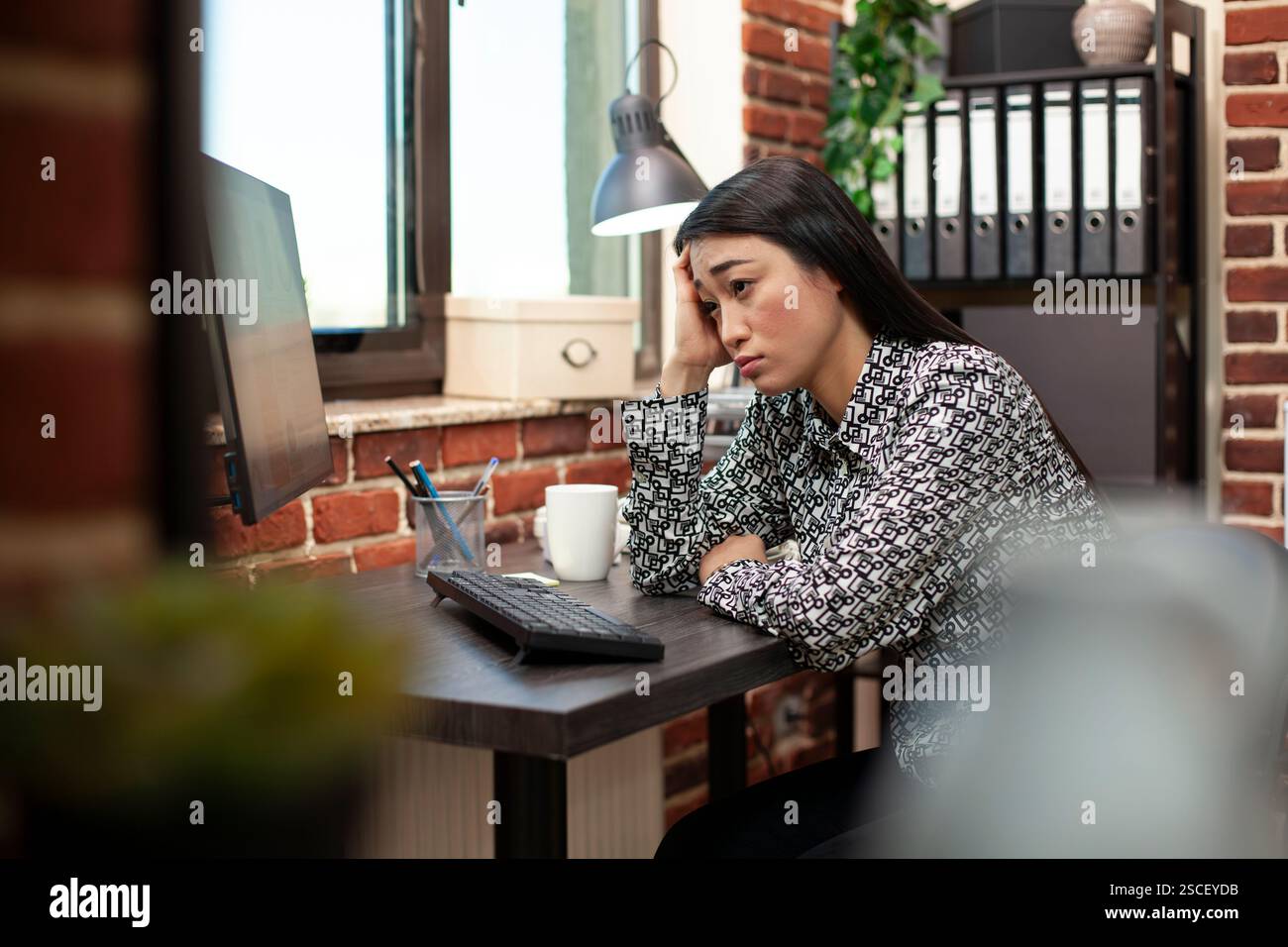 Tired businesswoman sitting at desk, face in hand, struggling to focus ...