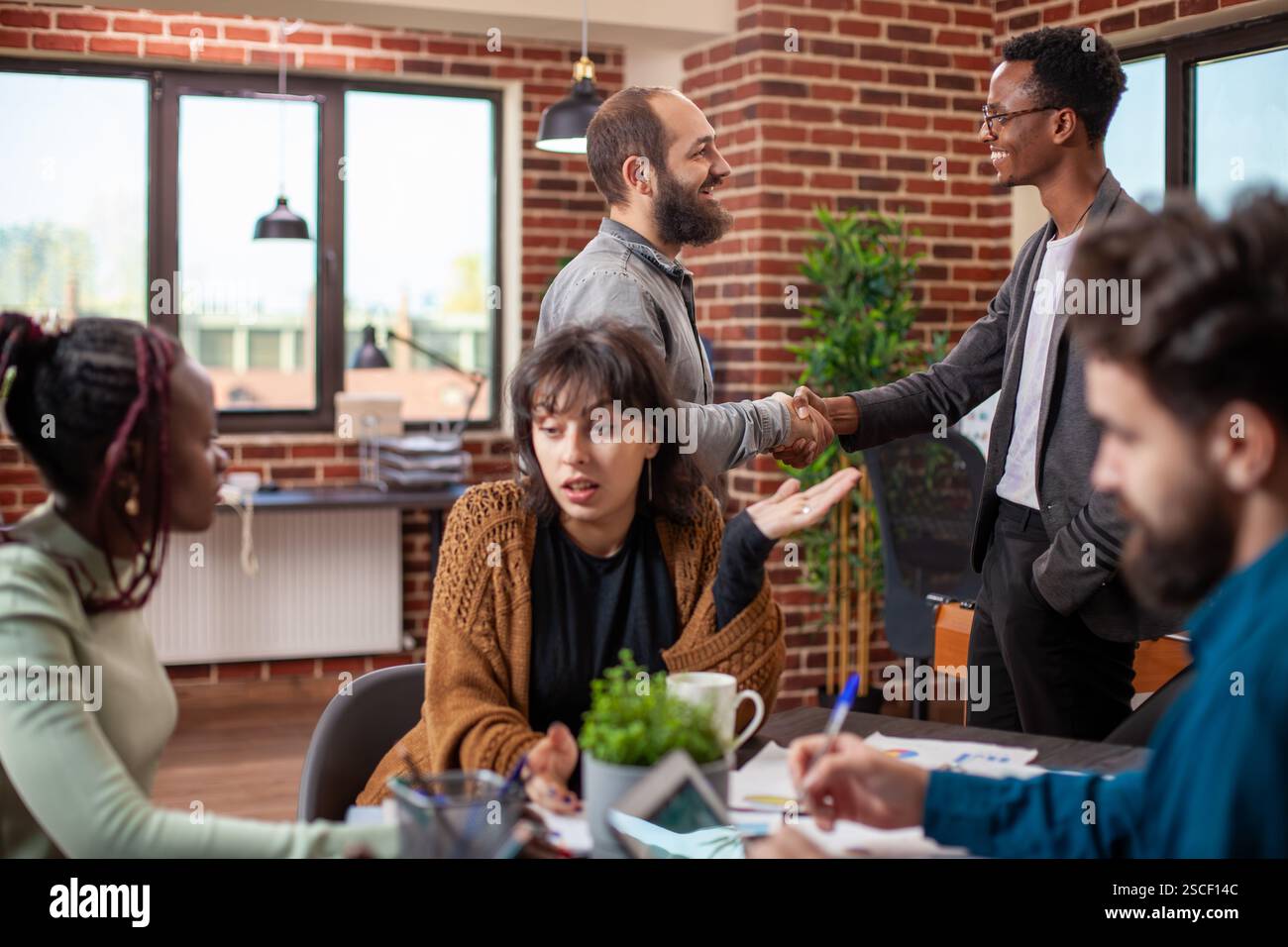 Bearded man shakes hands with African American manager in brick wall ...