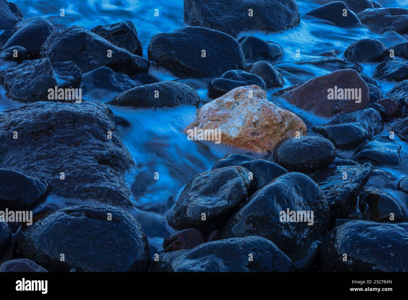 Long-exposure, black volcanic rocks, a single lighter-coloured stone ...