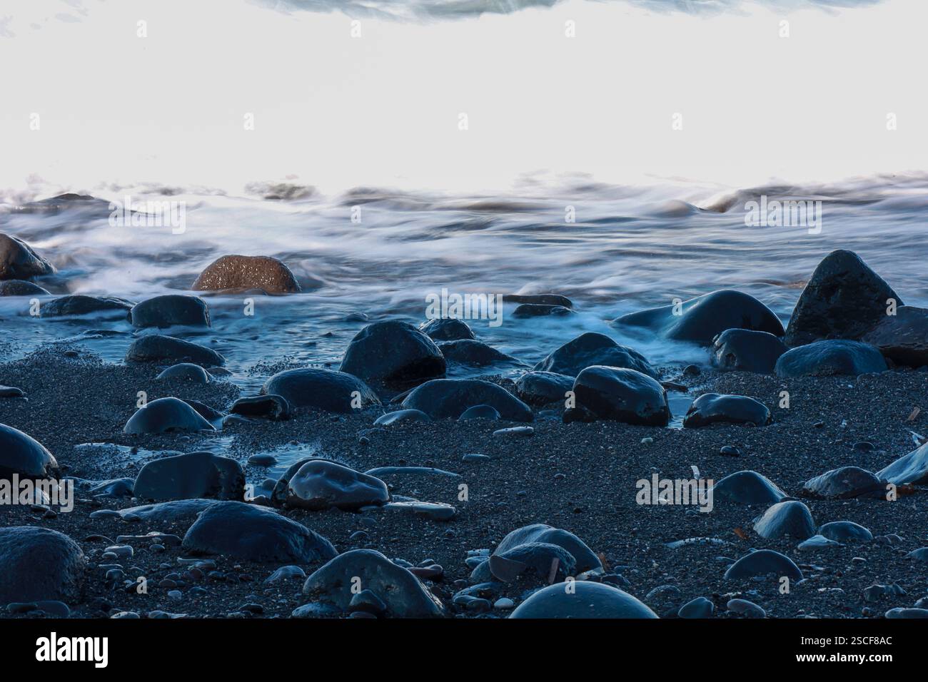 Long-exposure, black volcanic rocks, a single lighter-coloured stone ...