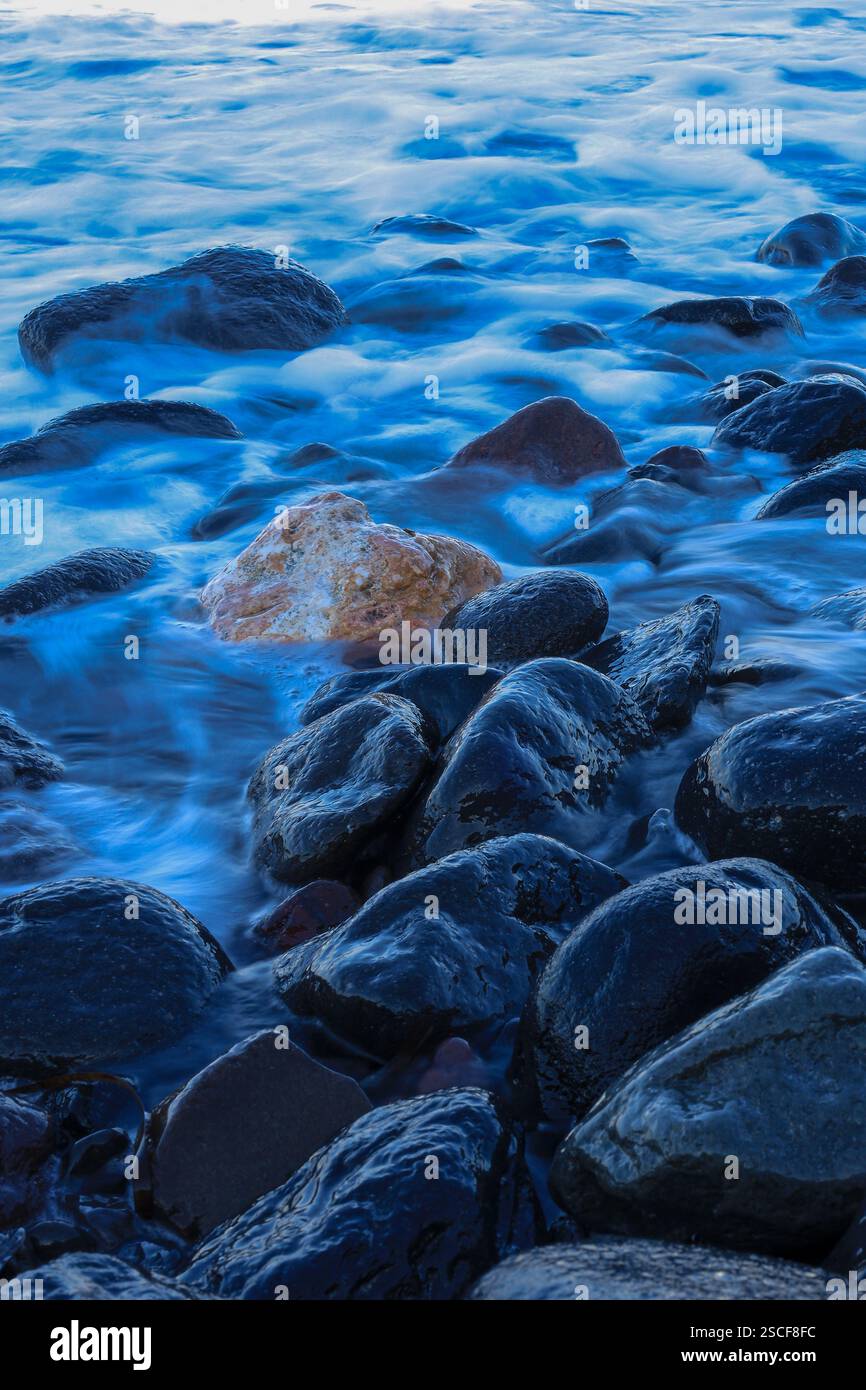 Long-exposure, black volcanic rocks, a single lighter-coloured stone ...