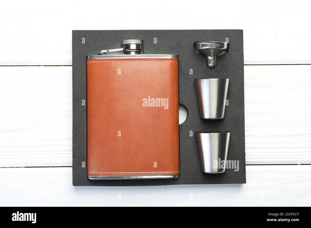 Hip flask, cups and funnel in package on white wooden table, top view ...