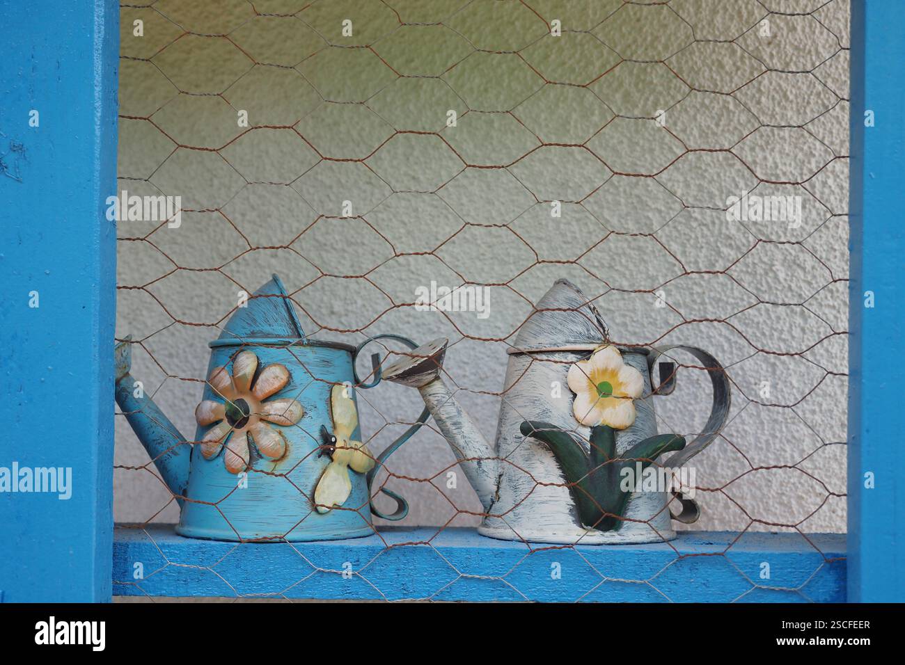Decorative watering cans displayed on a shelf behind mesh wire Stock ...