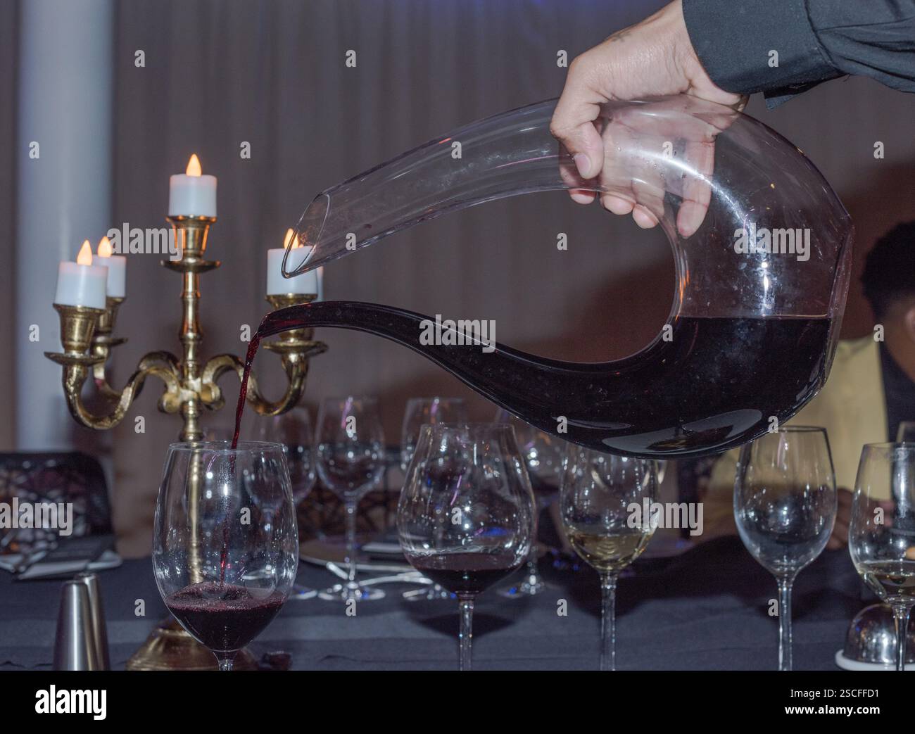 Hand pouring red wine from carafe into wine glasses in front of brass ...