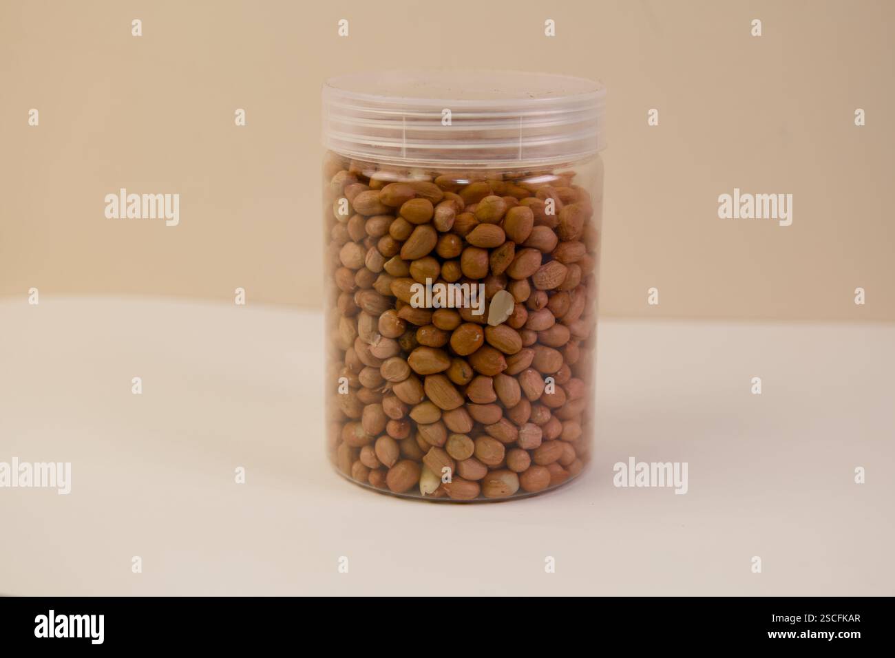 A transparent plastic container is filled with uncooked peanuts. The ...