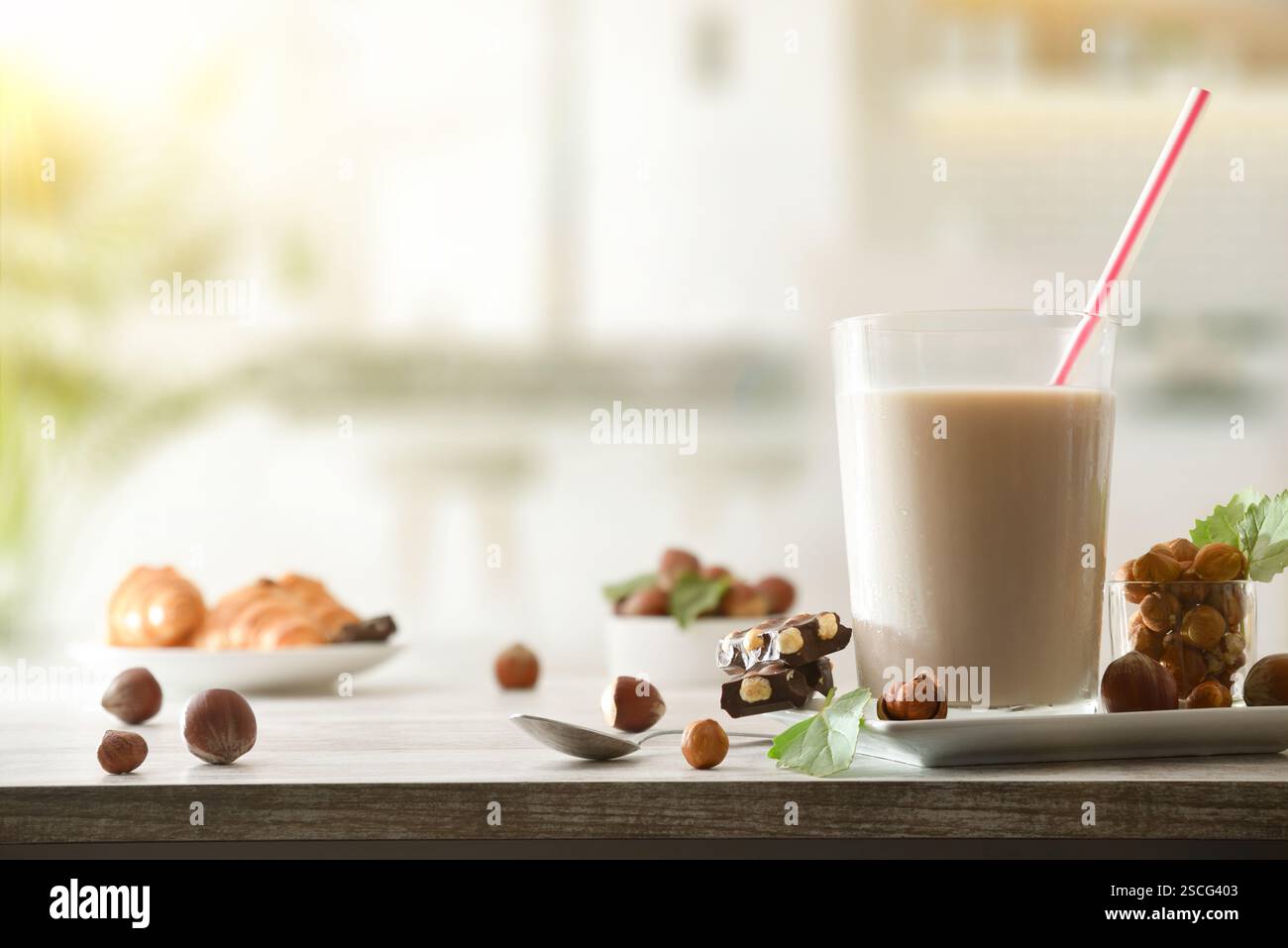 Glass of hazelnut drink with straw on kitchen bench with fruits and ...