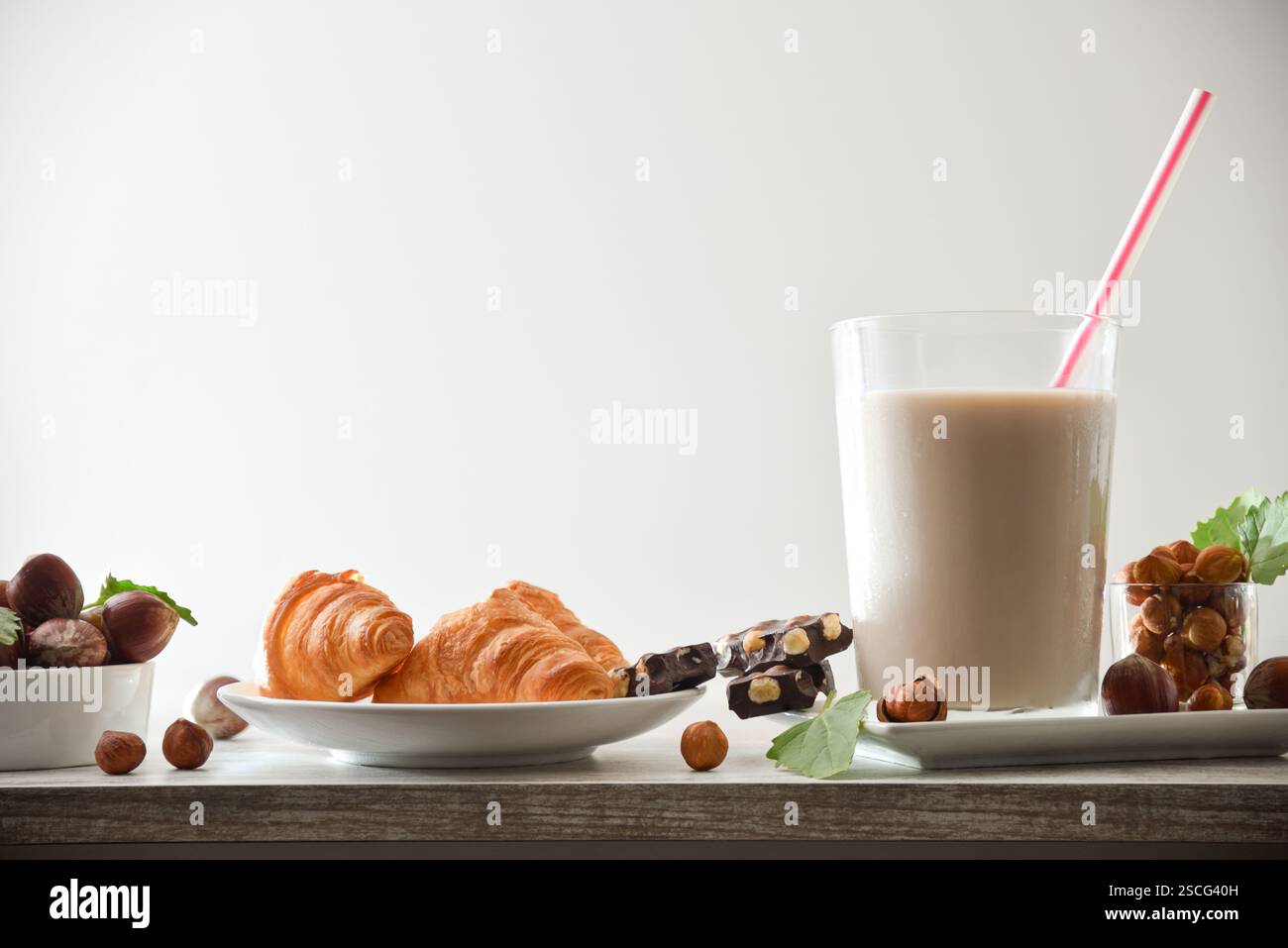 Glass of hazelnut drink with straw on wooden kitchen bench with fruits ...