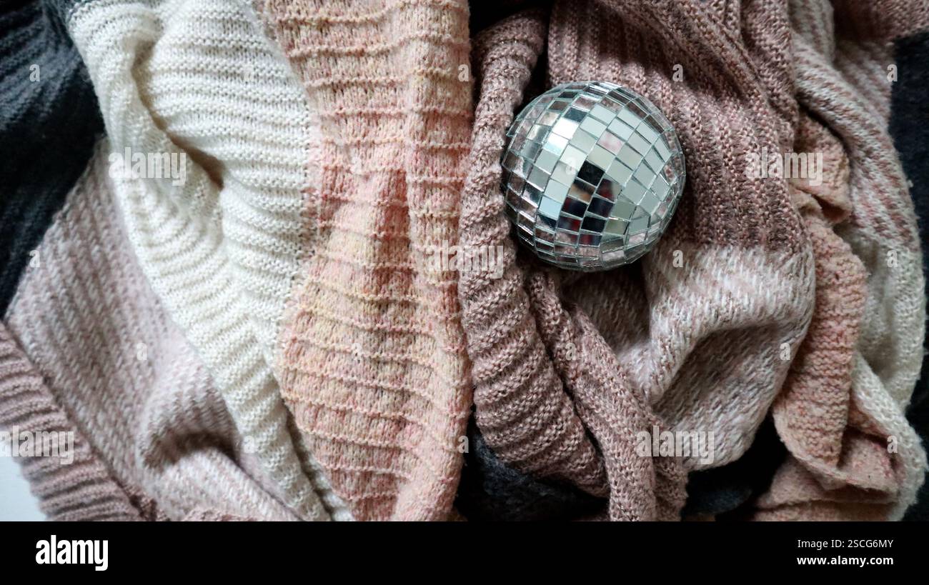Disco ball lies on soft material. Knitted fabric is chaotically folded ...