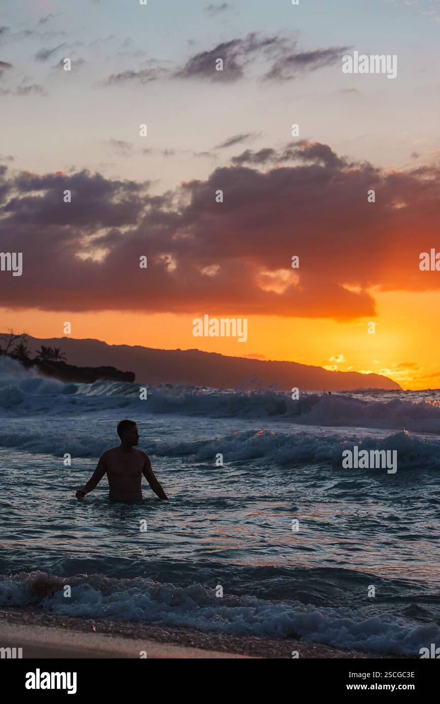 Silhouetted Figure in Ocean at Sunset with Tree Lined Cliffs Stock ...