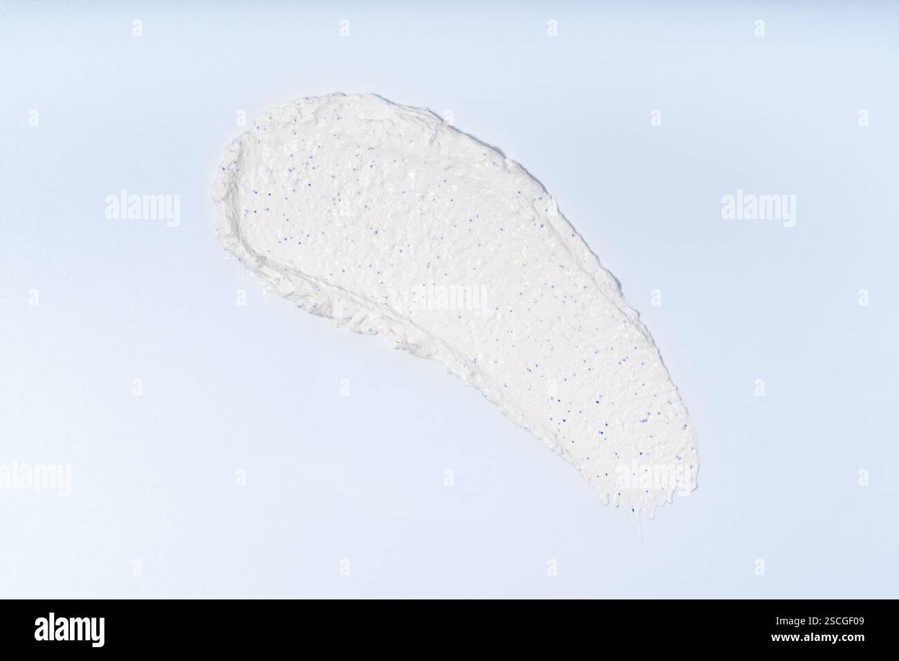 A white smear of face scrub on a light blue background, isolated smudge ...