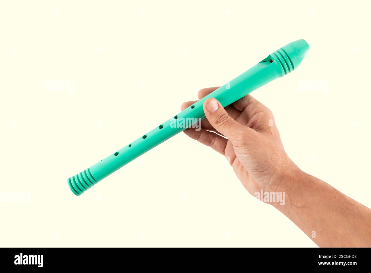 Male hand holding a green recorder flute isolated on light yellow ...