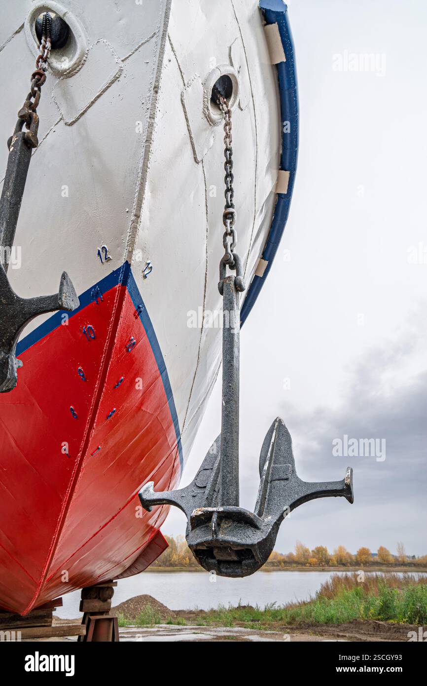 Ship's bow with a red and white hull, flanked by two large anchors on ...