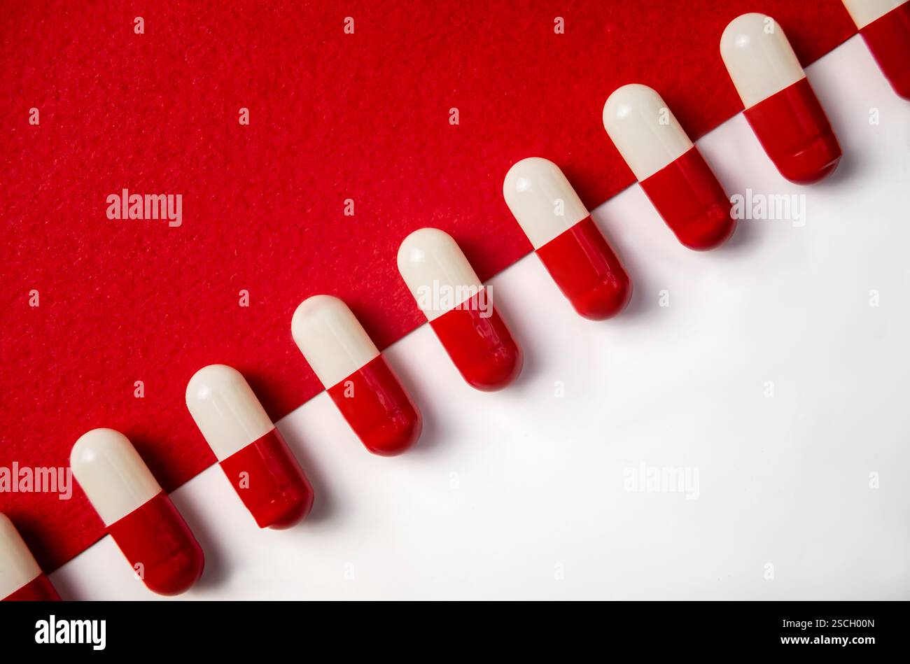 Red and white capsules lie in a neat line on a surface, highlighting ...