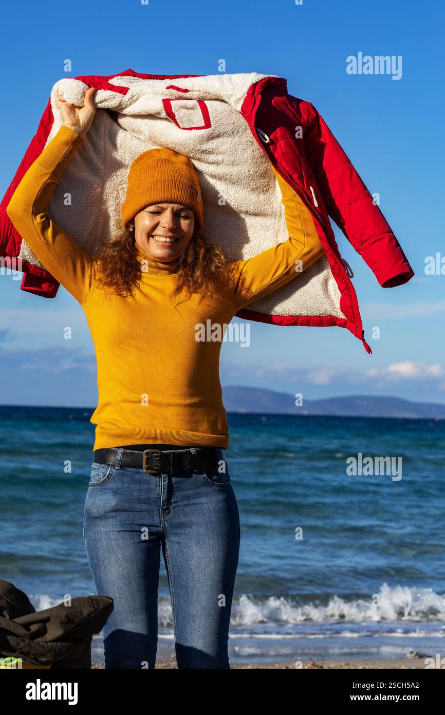 Happy young woman taking off jacket on a sunny day gainst sea and sky ...