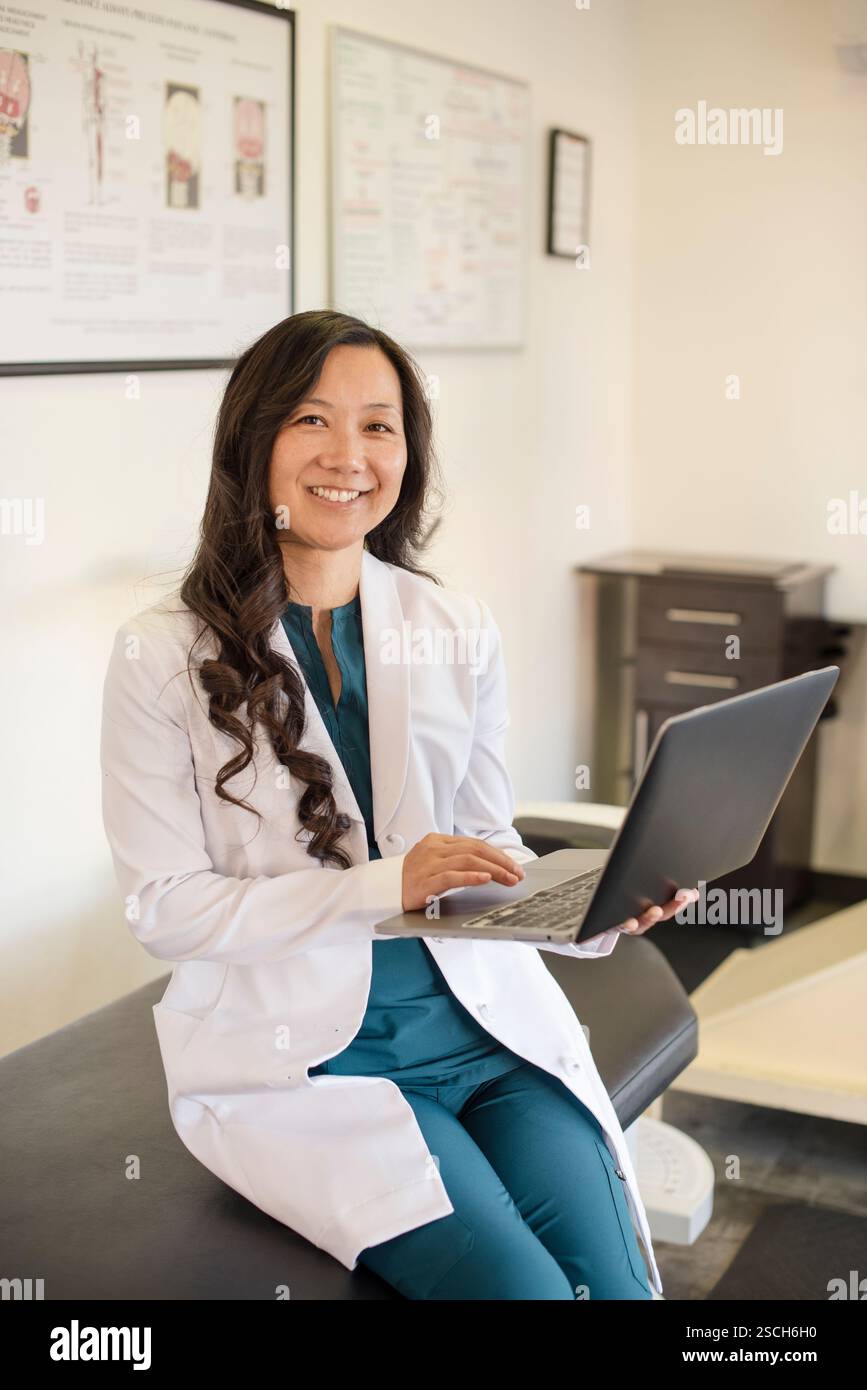 Woman doctor sitting down with laptop Stock Photo - Alamy