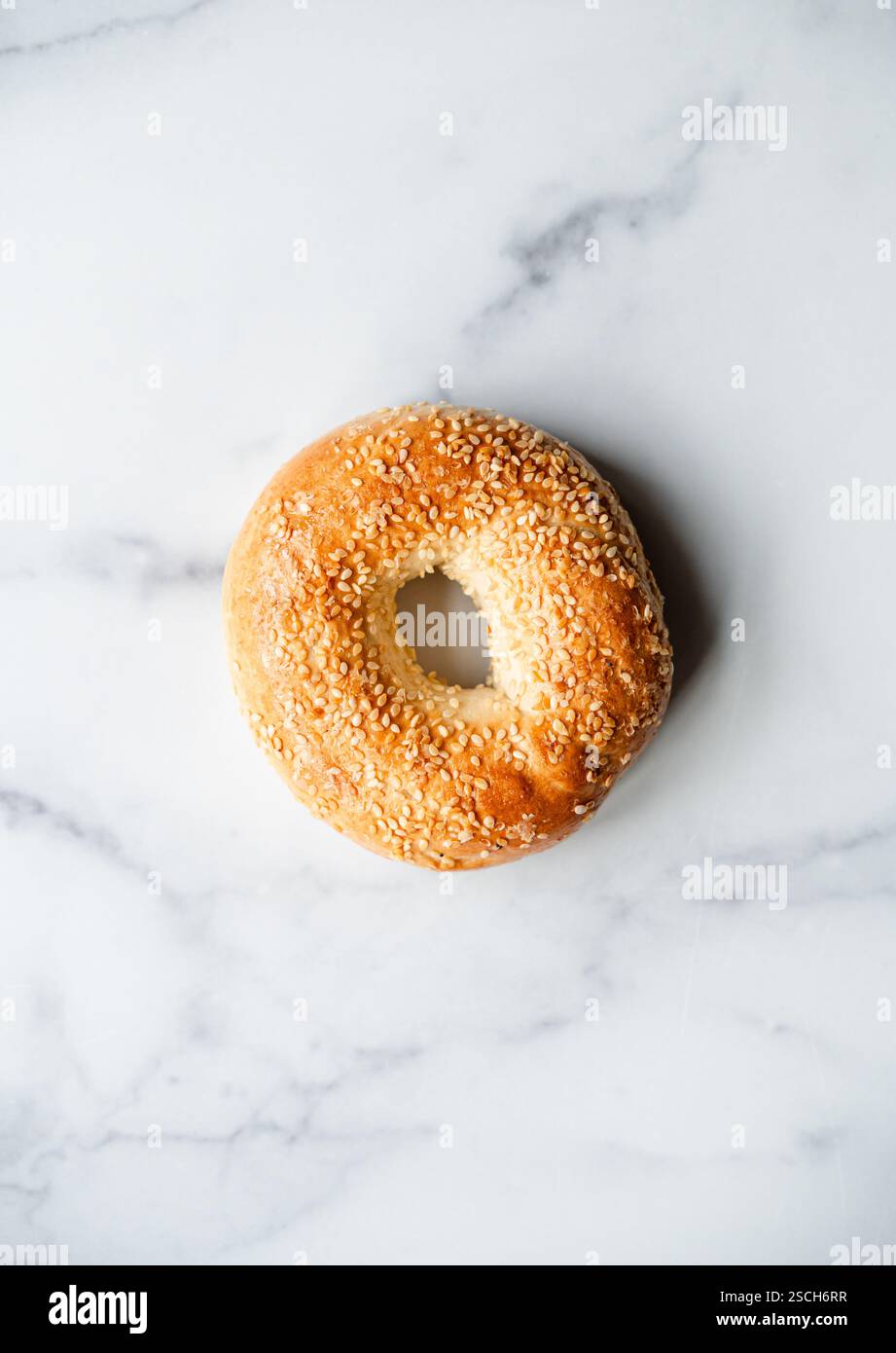 Top view of single sesame seed bagel against white marble background ...