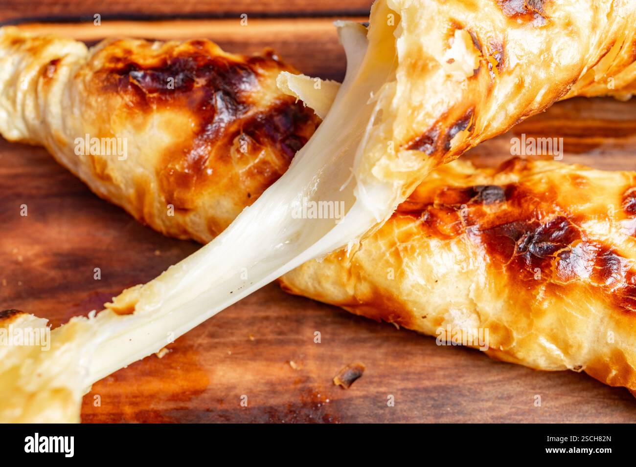 Flaky pastry filled with melted cheese is pulled apart, revealing its ...