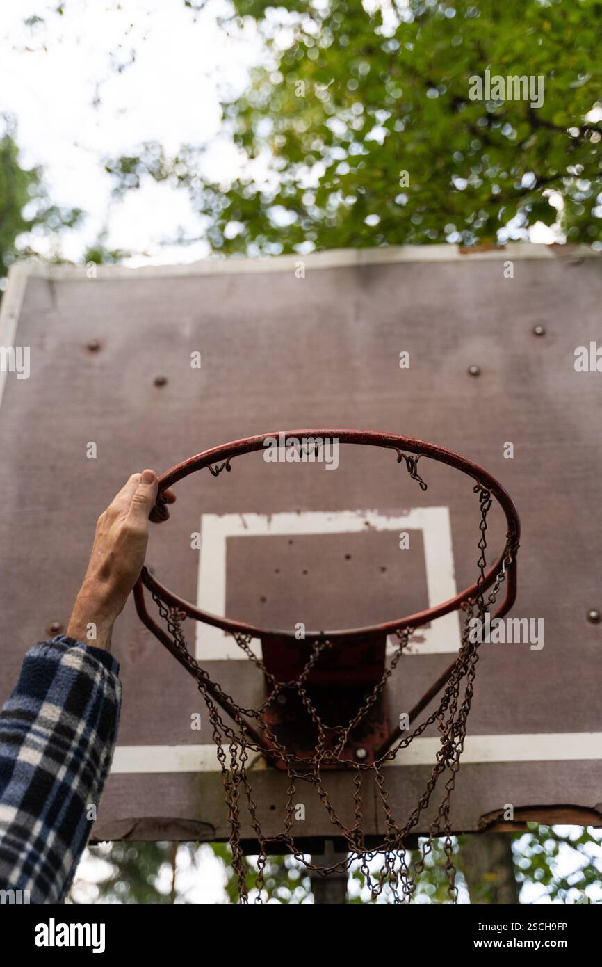 A hand reaches up to grab an old, iron basketball hoop with a chain net ...