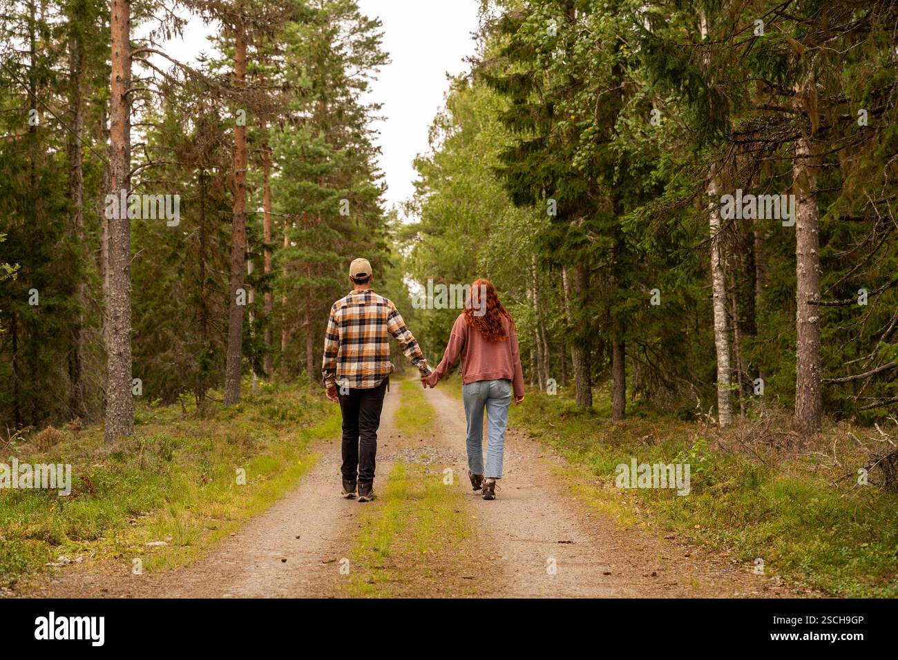 A couple walks down a serene forest path in Sweden, holding hands and ...