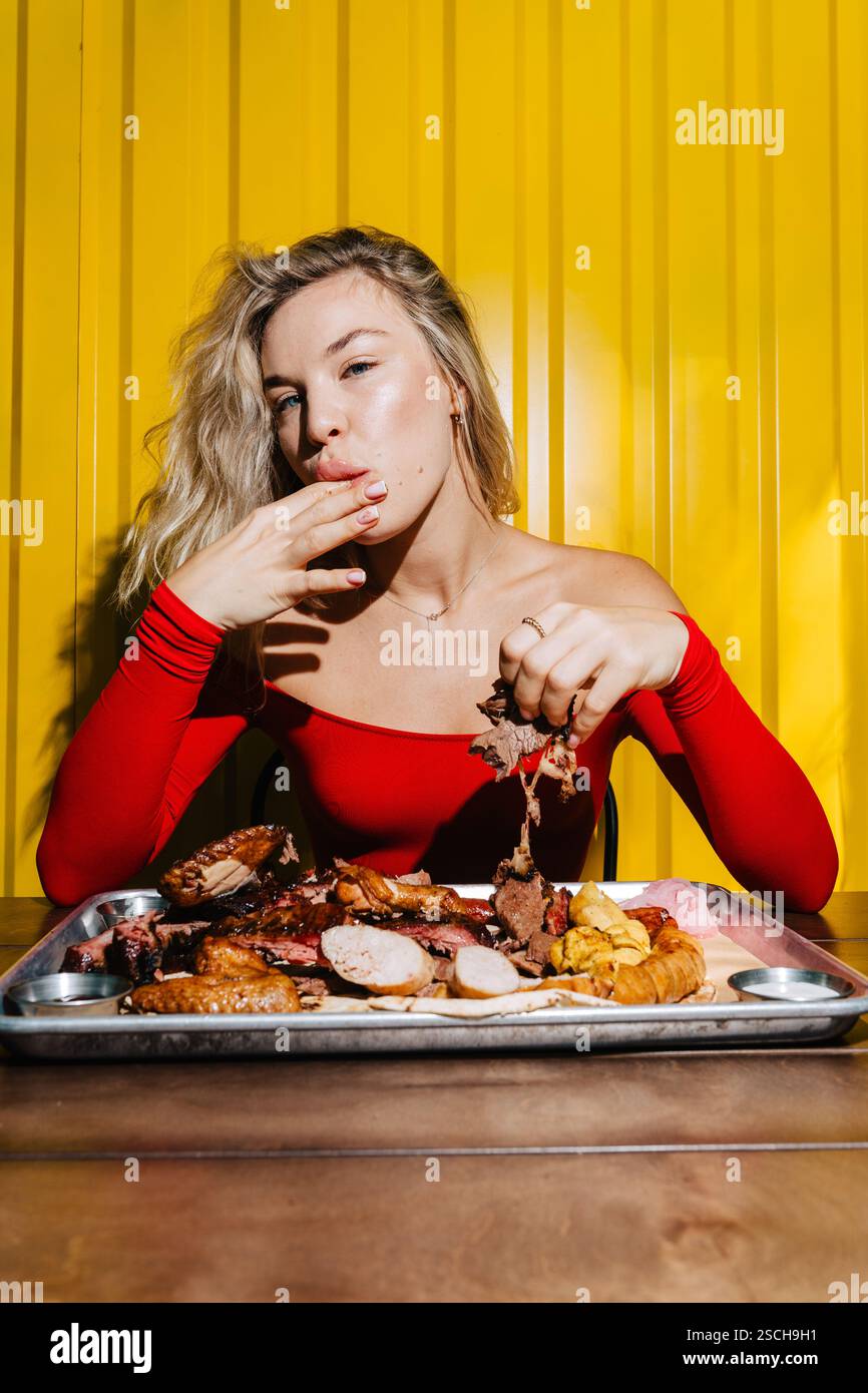 A woman in a vibrant red outfit relishes assorted barbecued meats on a ...