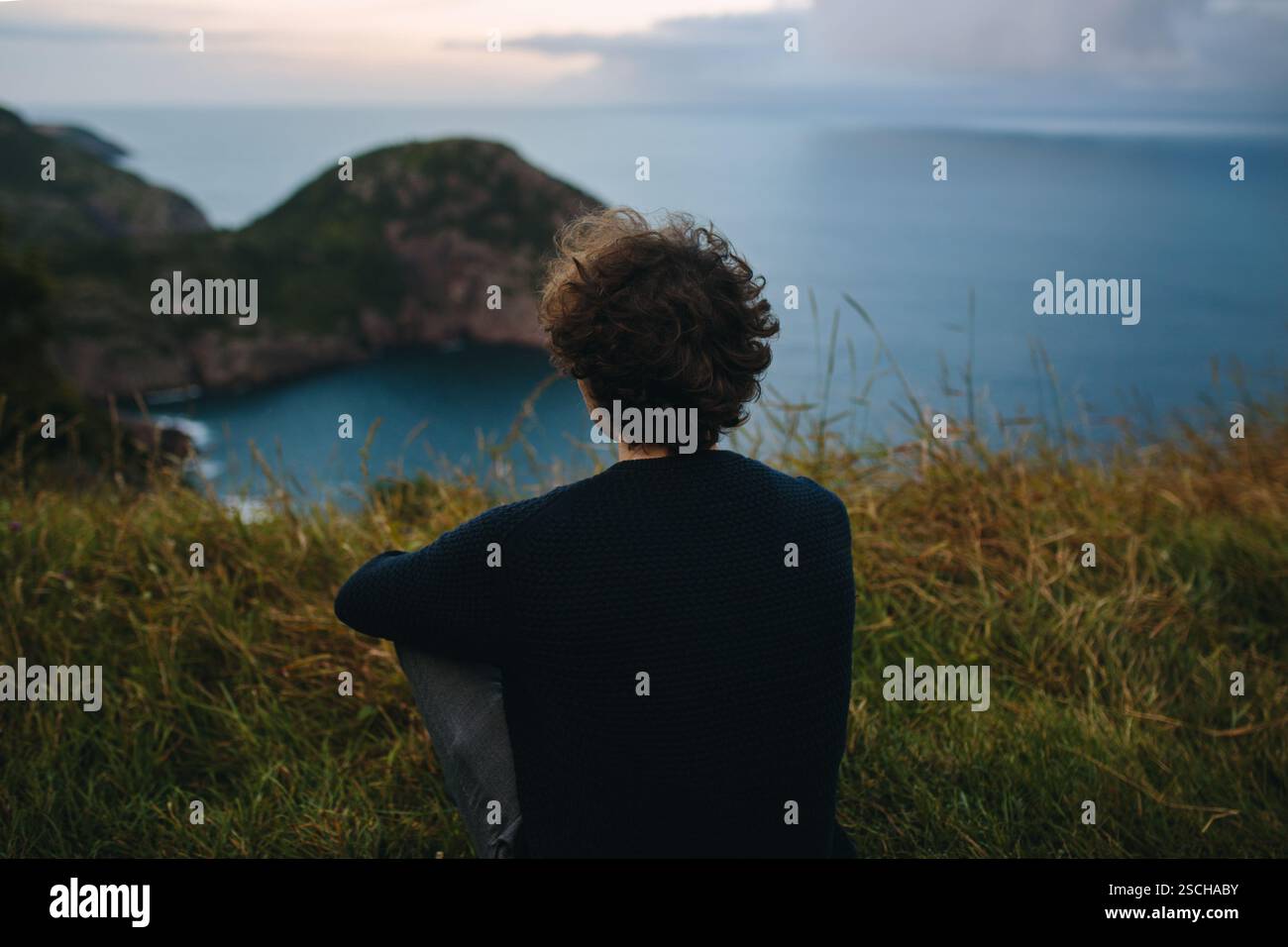 Back view of unrecognizable person sitting on grassy hill, overlooking ...