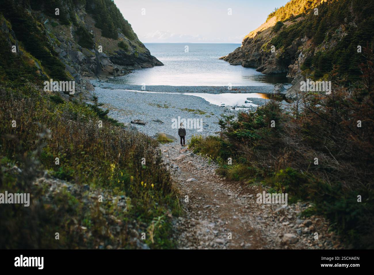 Back view of an unrecognizable man descending a rugged trail towards a ...