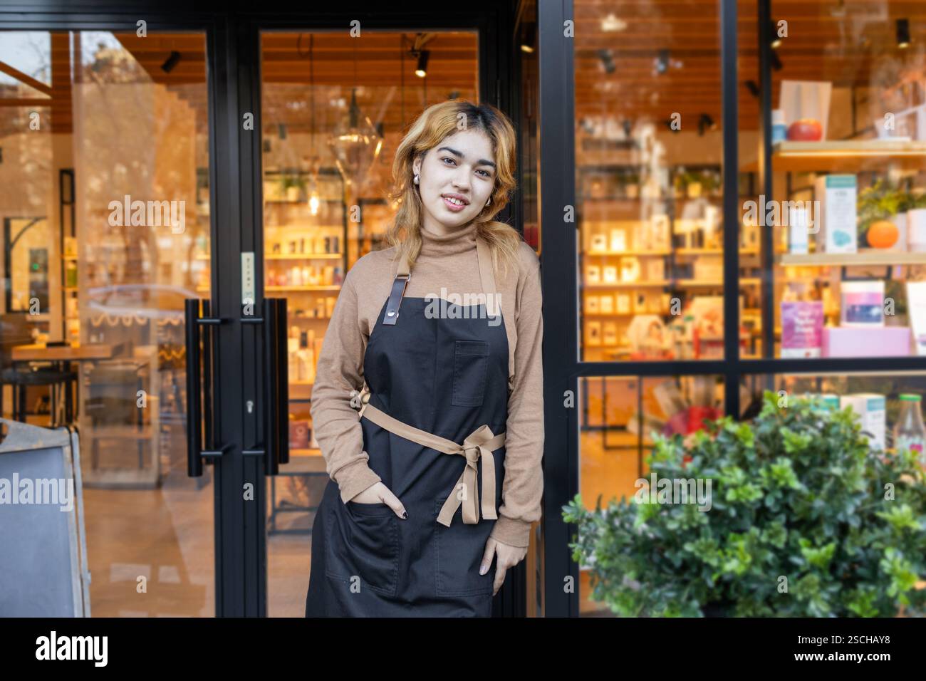 A welcoming employee stands outside a cosmetics store, wearing an apron ...