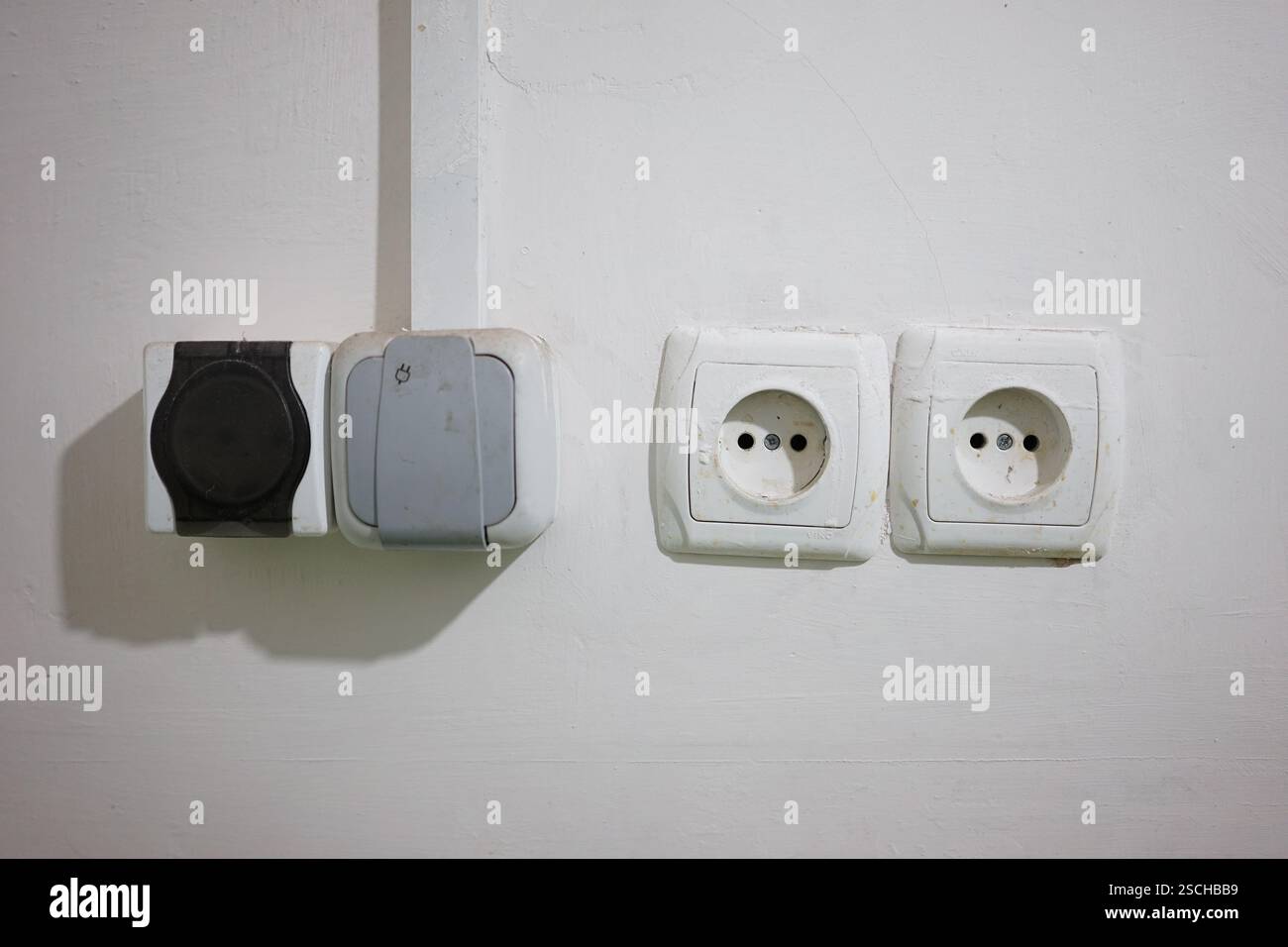 Two electrical outlets and a switch are mounted on a simple white wall ...