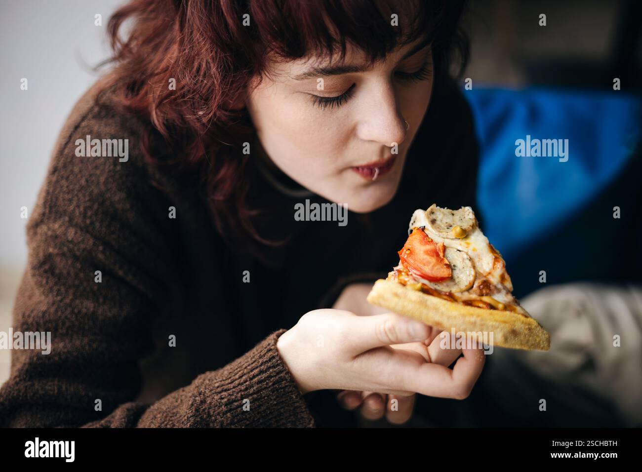 A young adult woman with curly red hair enjoys a delicious slice of ...