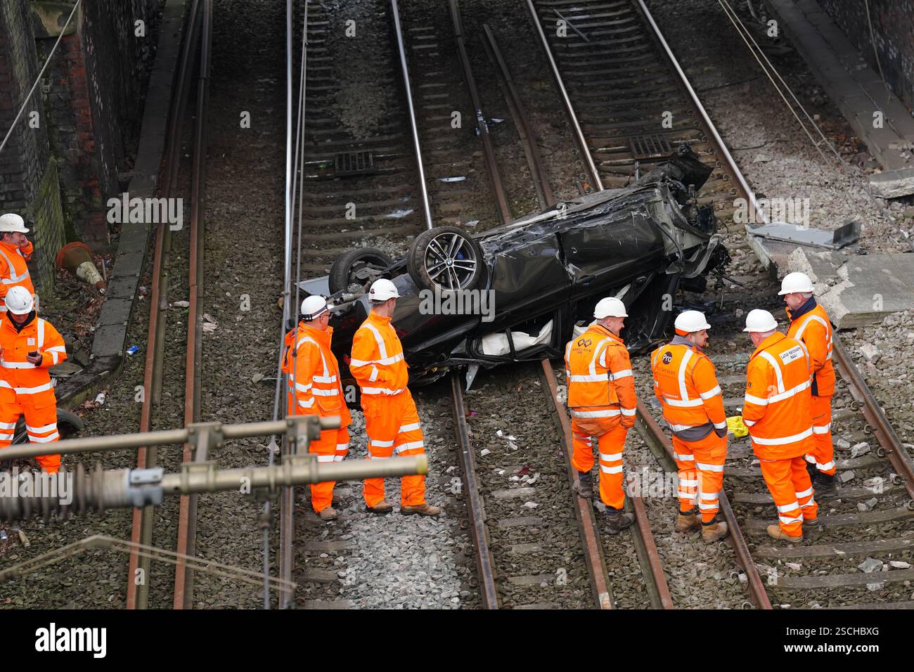 Emergency workers view a car that crashed onto tracks in Salford ...