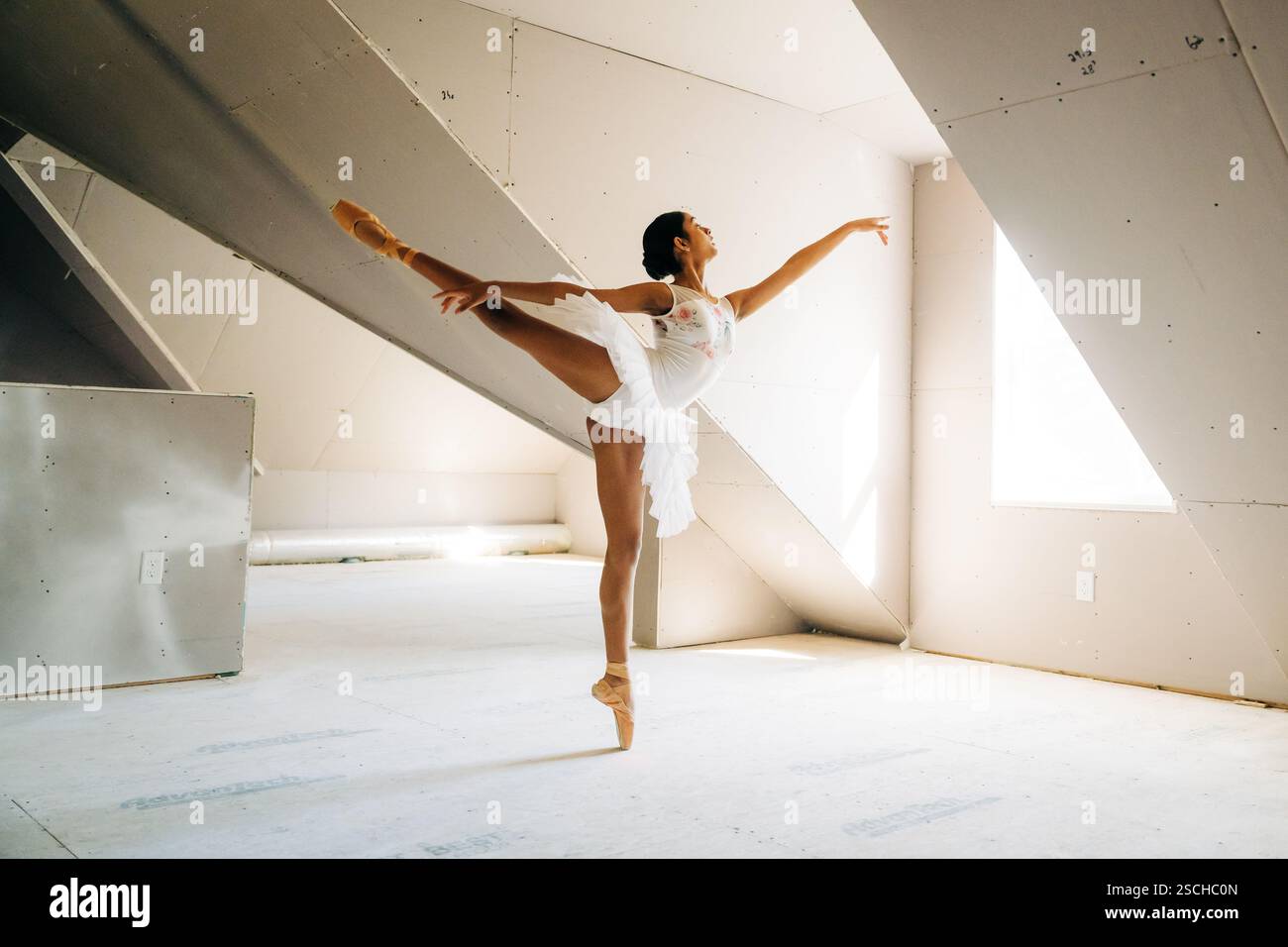 Ballerina en pointe in an arabesque pose, gracefully lit in a loft ...