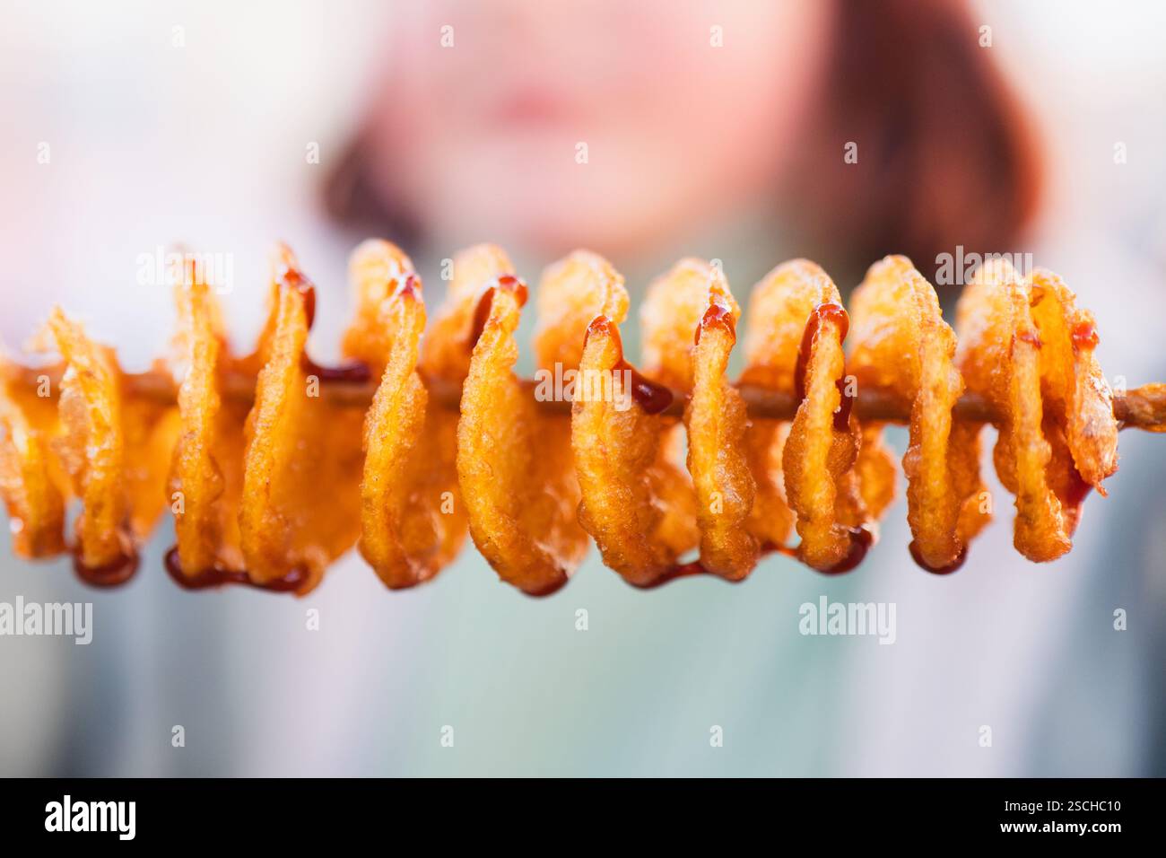 Close-up of golden spiral tornado potatoes on a stick, drizzled with ...