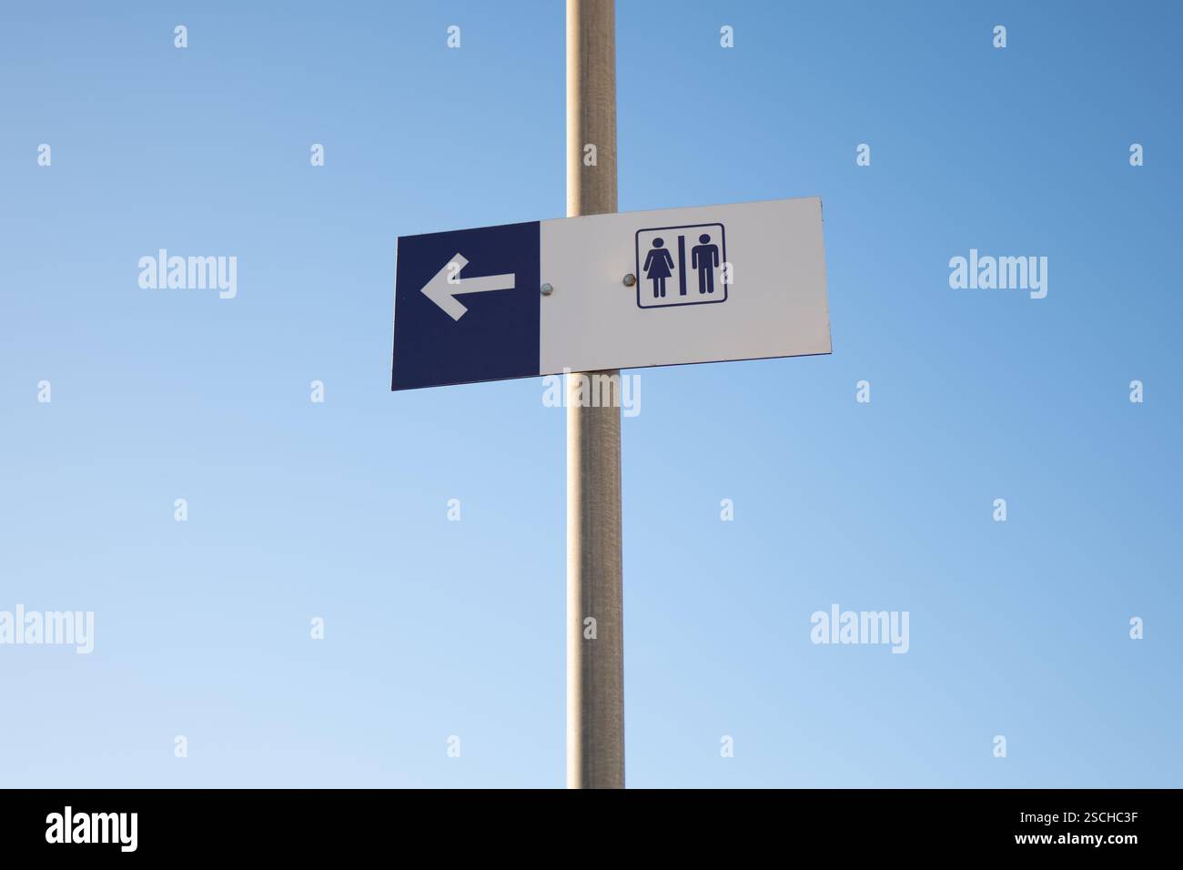 A restroom direction sign on a pole pointing left, set against a clear ...
