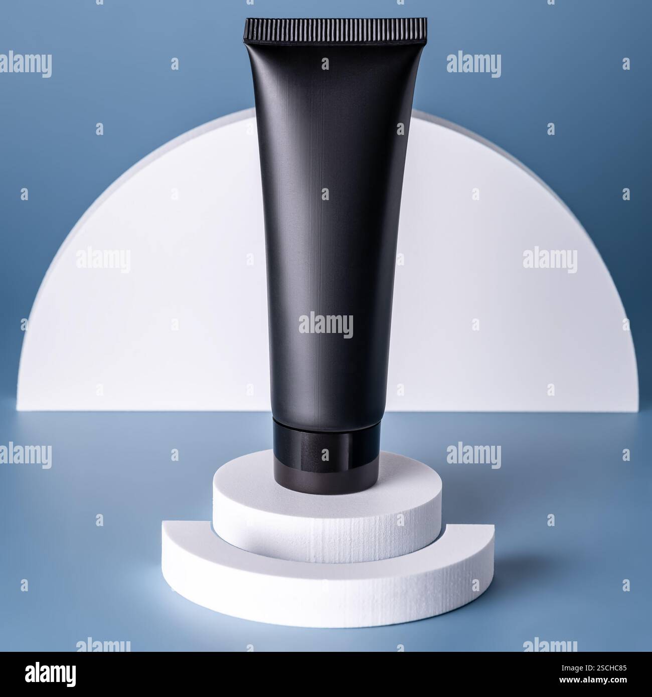 A sleek black cosmetic tube stands atop layered white circular podiums ...