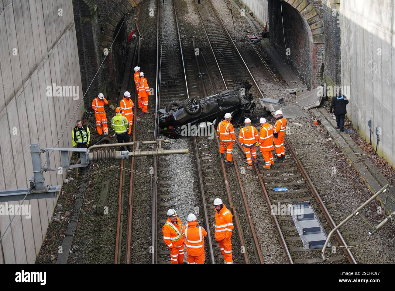 Emergency workers view a car that crashed onto tracks in Salford ...