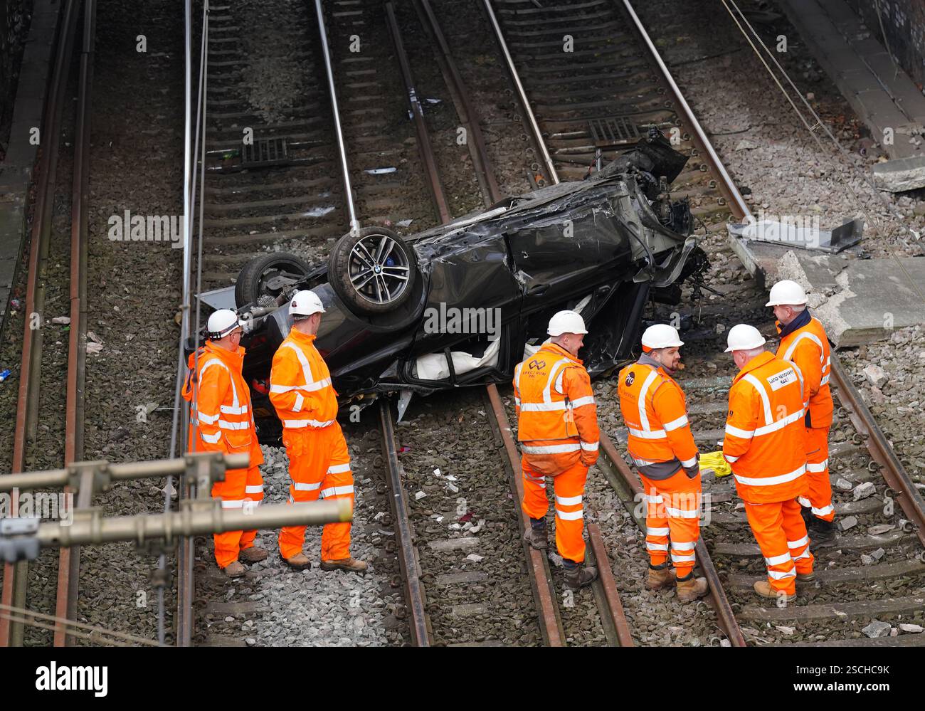 Emergency workers view a car that crashed onto tracks in Salford ...