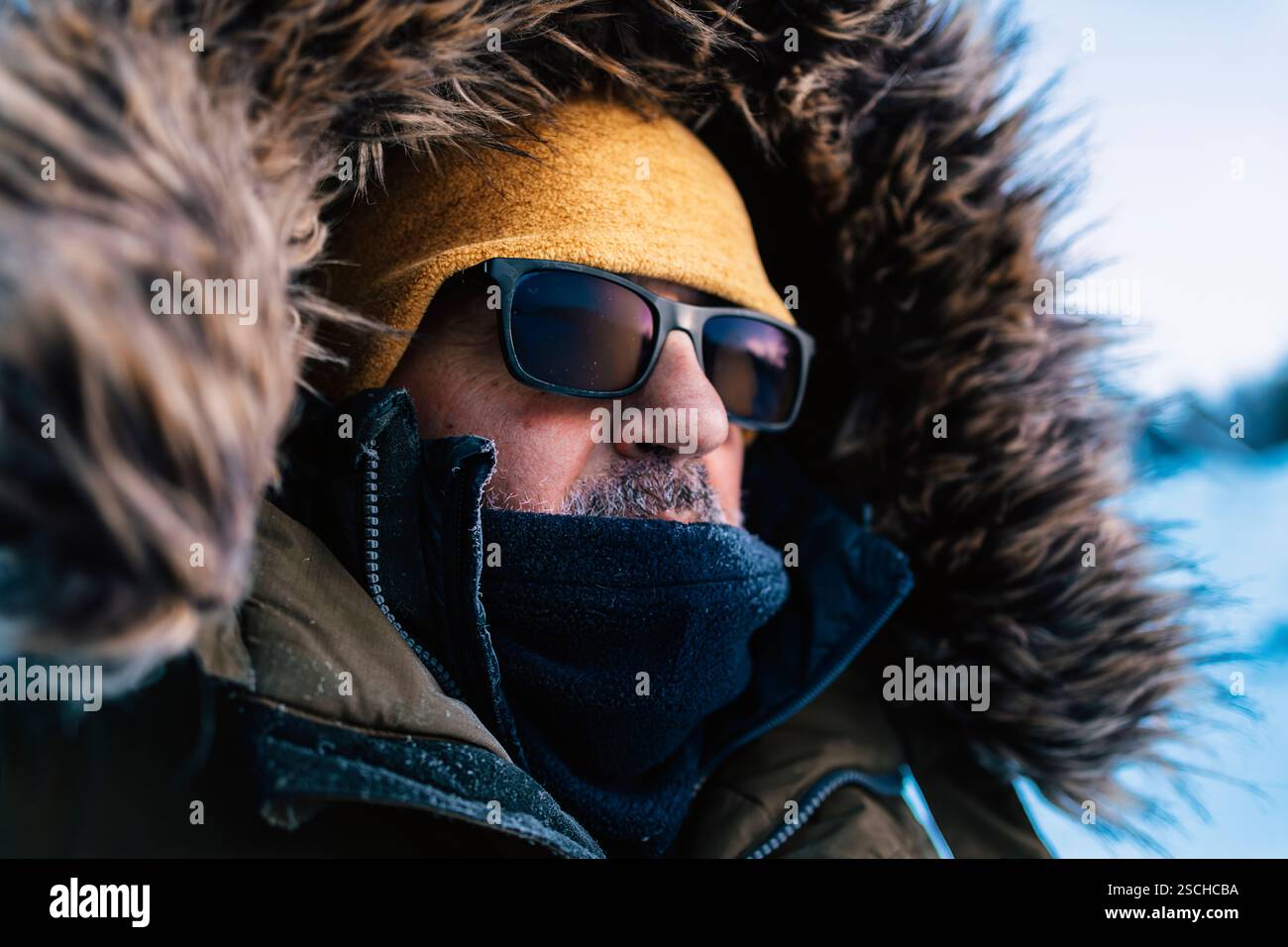 An adventurer warmly dressed in a fur-lined hood and sunglasses faces ...